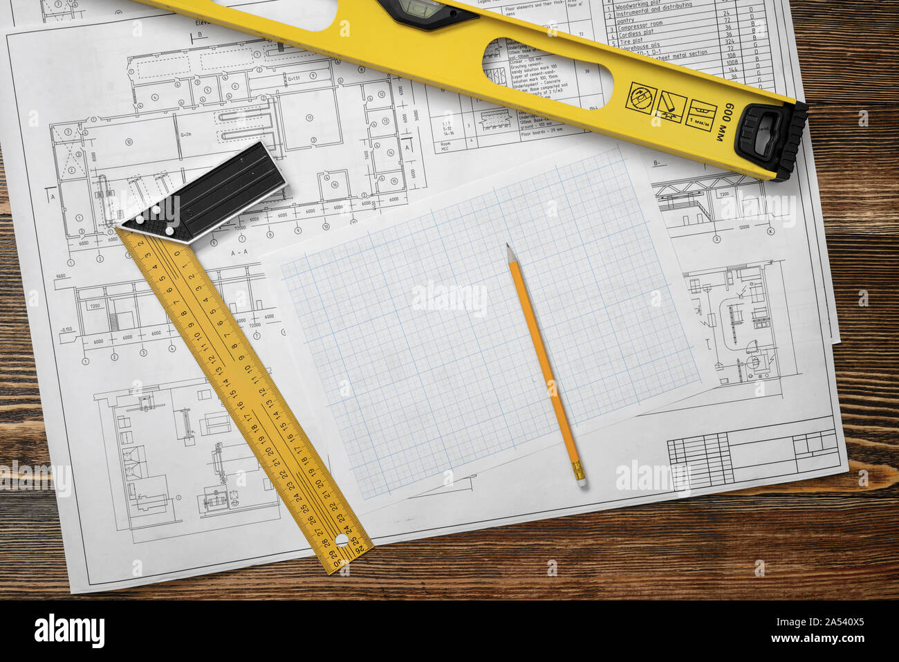 Wooden table with blueprints, a ruler with angle bar, a builders level ...