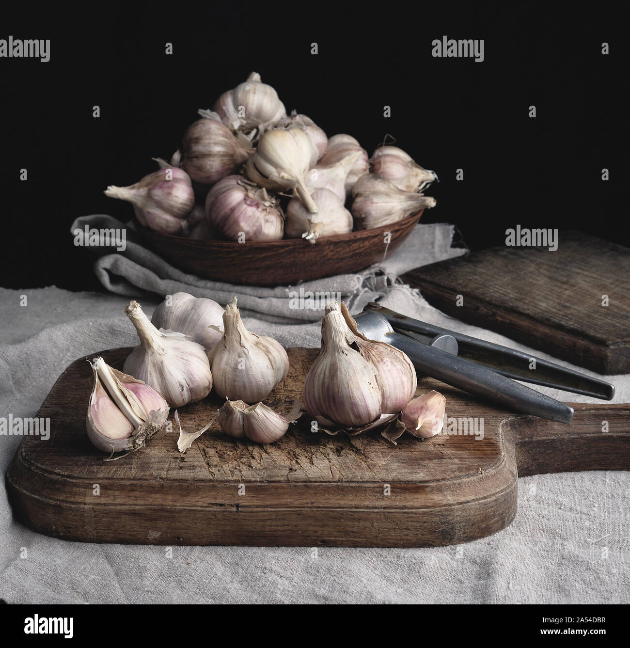 raw unpeeled garlic on a very old vintage cutting board and iron pres ...