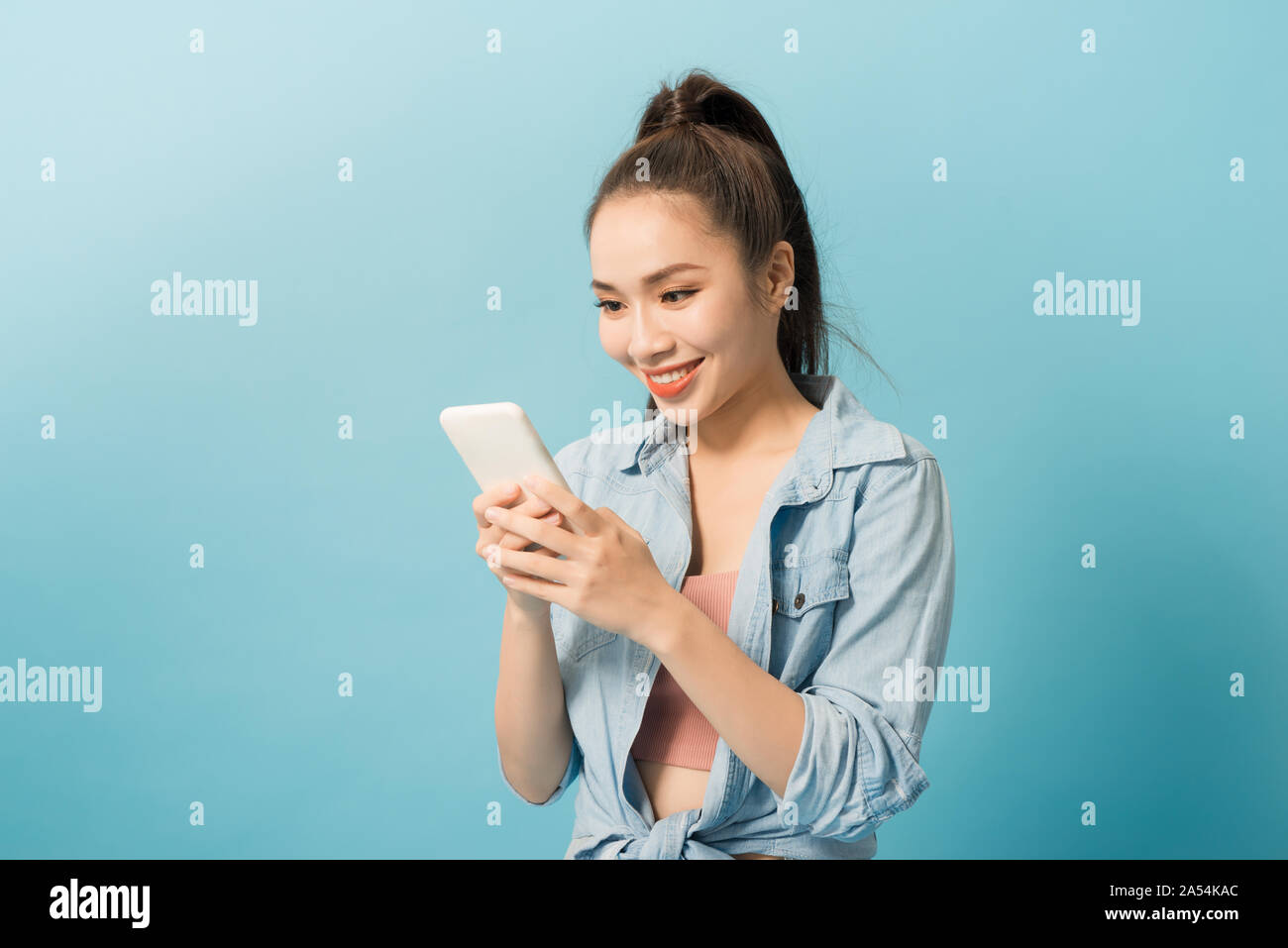 Asian woman 20s holding mobile phone and smiling over blue background ...