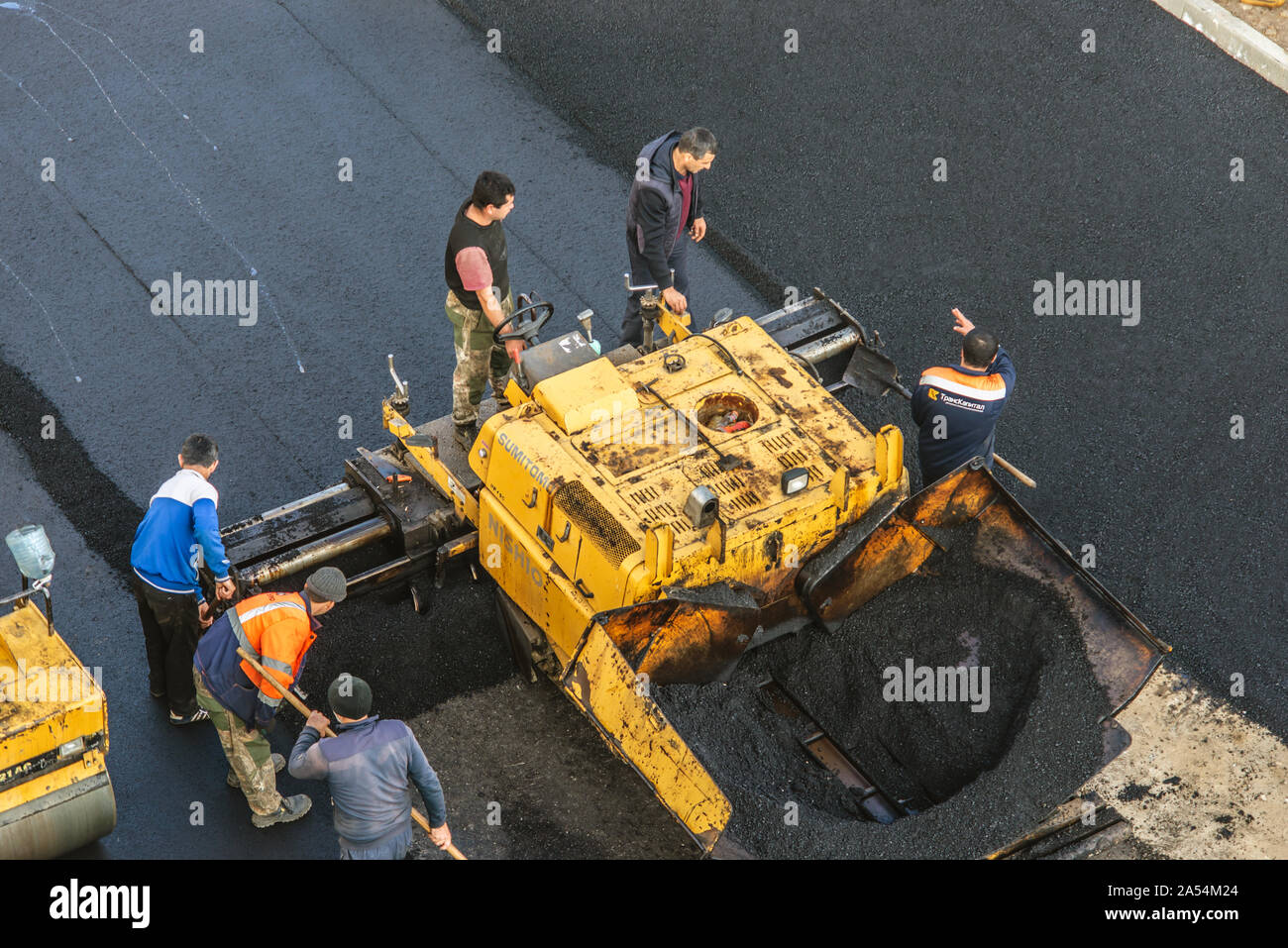 Workers lay a new asphalt coating using hot bitumen. Work of heavy ...