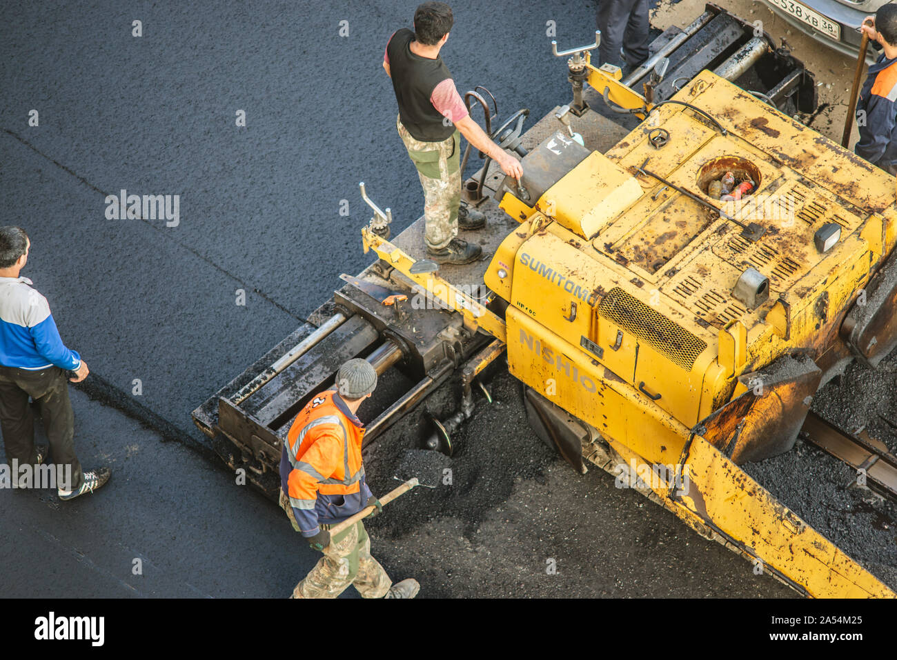 Workers lay a new asphalt coating using hot bitumen. Work of heavy ...