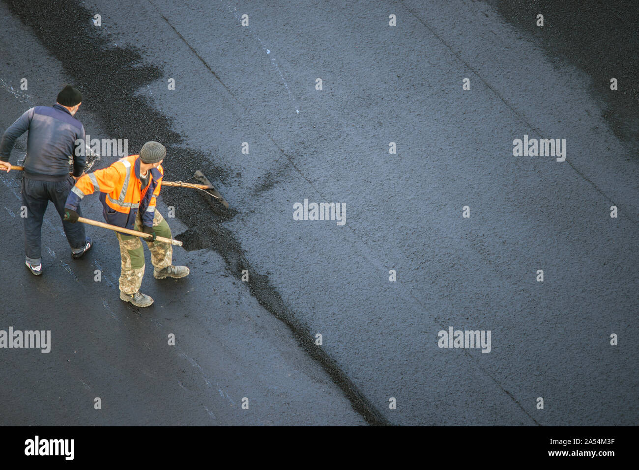 Workers lay a new asphalt coating using hot bitumen. Work of heavy ...