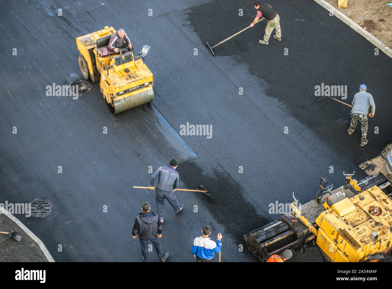 Workers lay a new asphalt coating using hot bitumen. Work of heavy ...