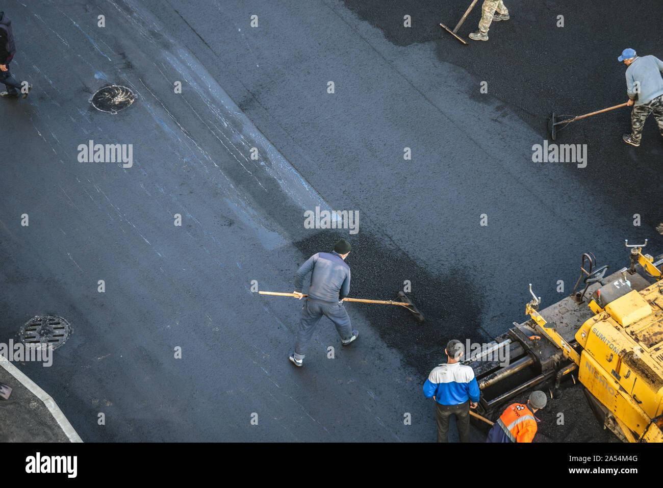 Workers lay a new asphalt coating using hot bitumen. Work of heavy ...