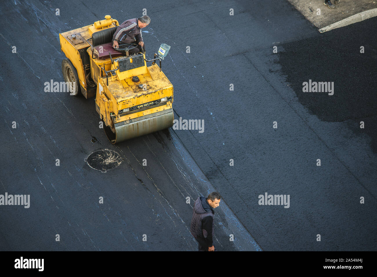 Workers lay a new asphalt coating using hot bitumen. Work of heavy ...
