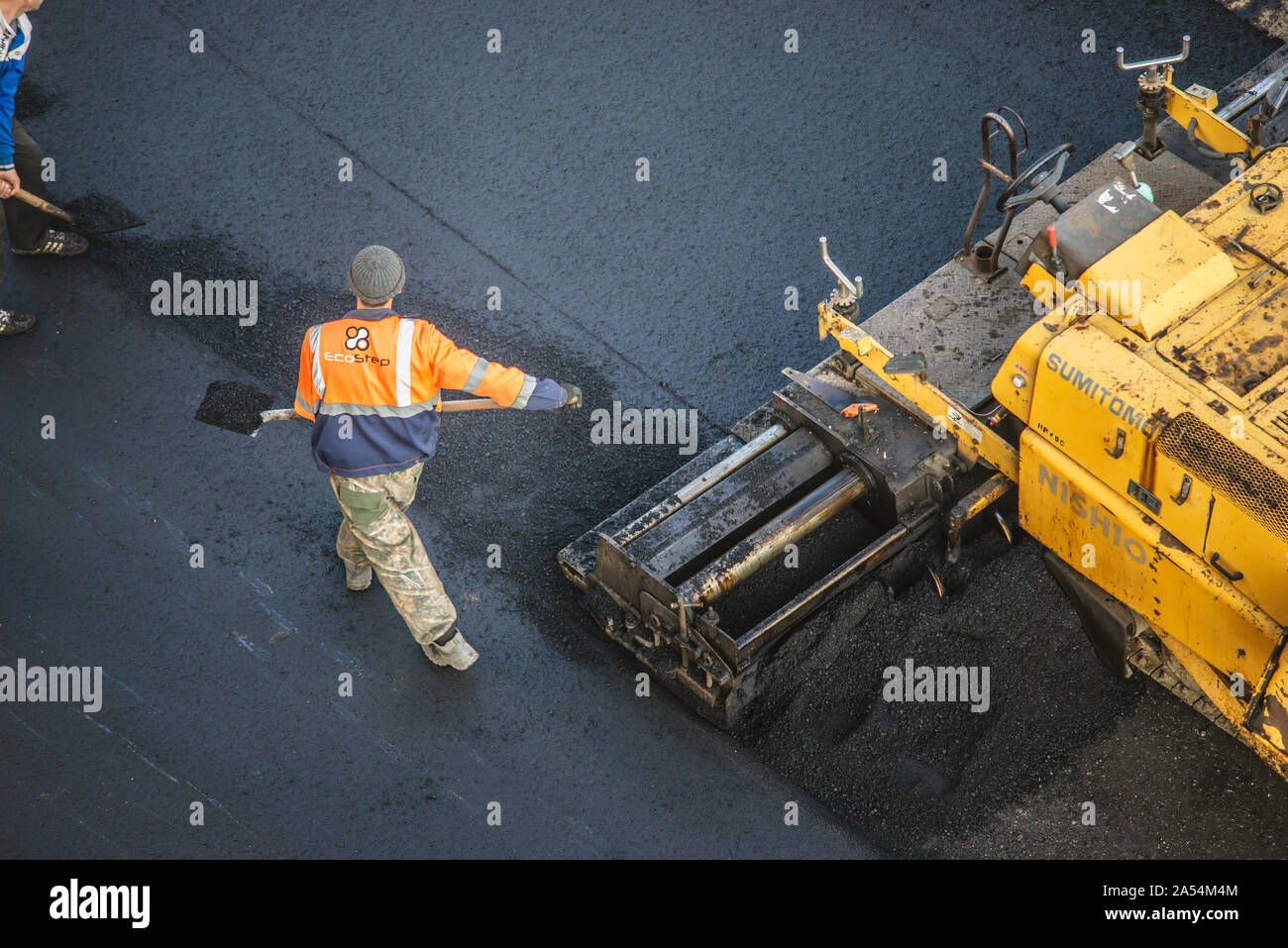 Workers lay a new asphalt coating using hot bitumen. Work of heavy ...