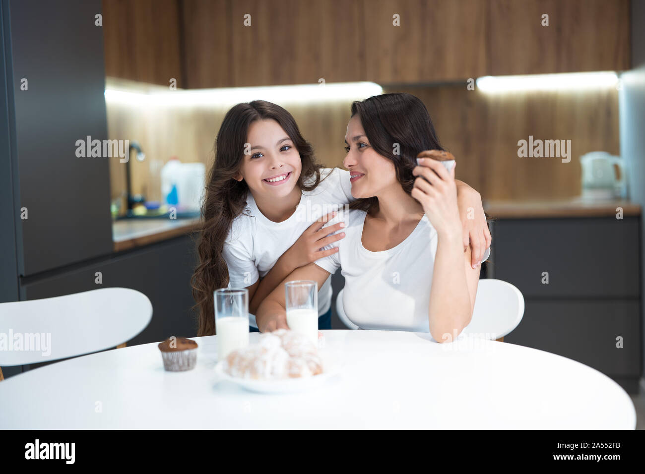 beautiful young mother with her cute teen daughter eating cupcakes and ...