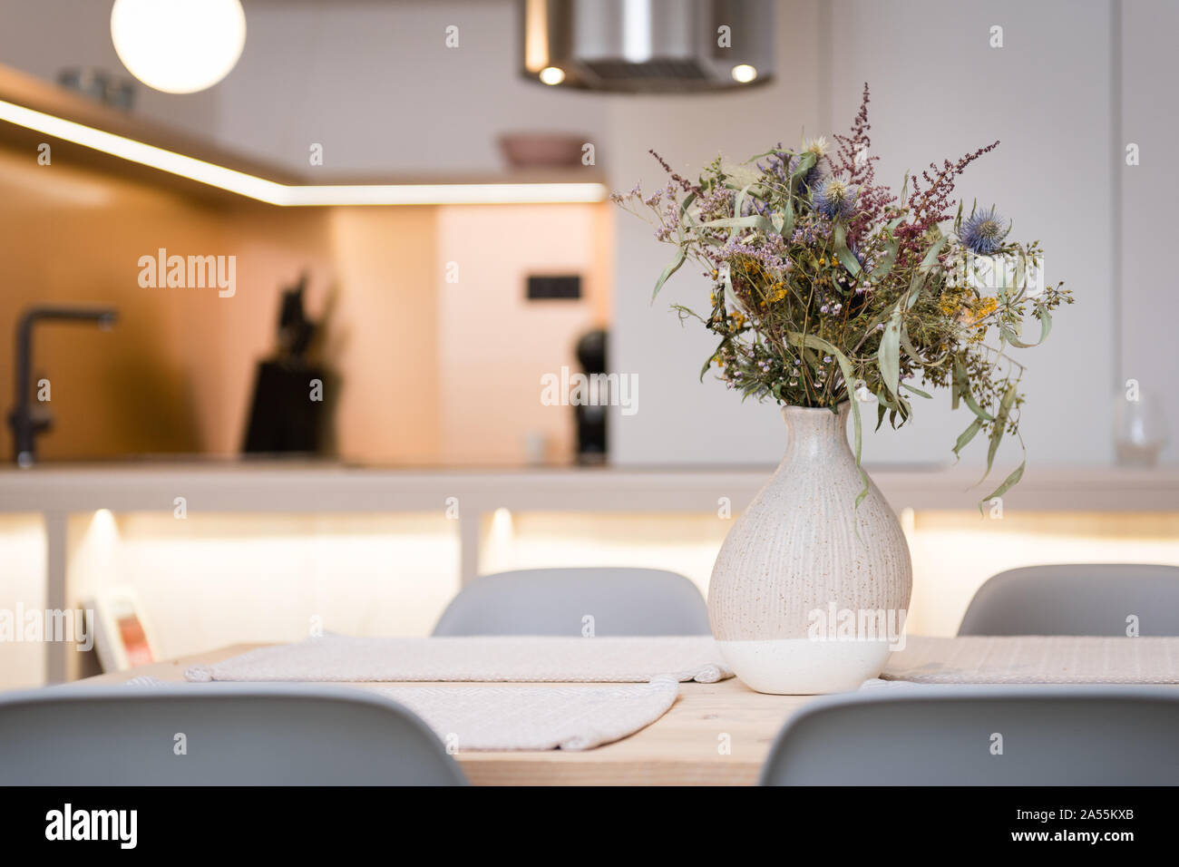 Vase on dining table of contemporary apartment, kitchen in background ...