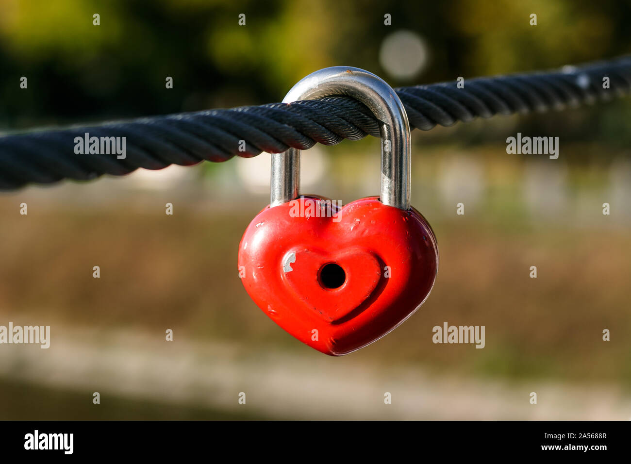 Red heart on a metal cable on bridge. Padlock of shape of heart on a ...