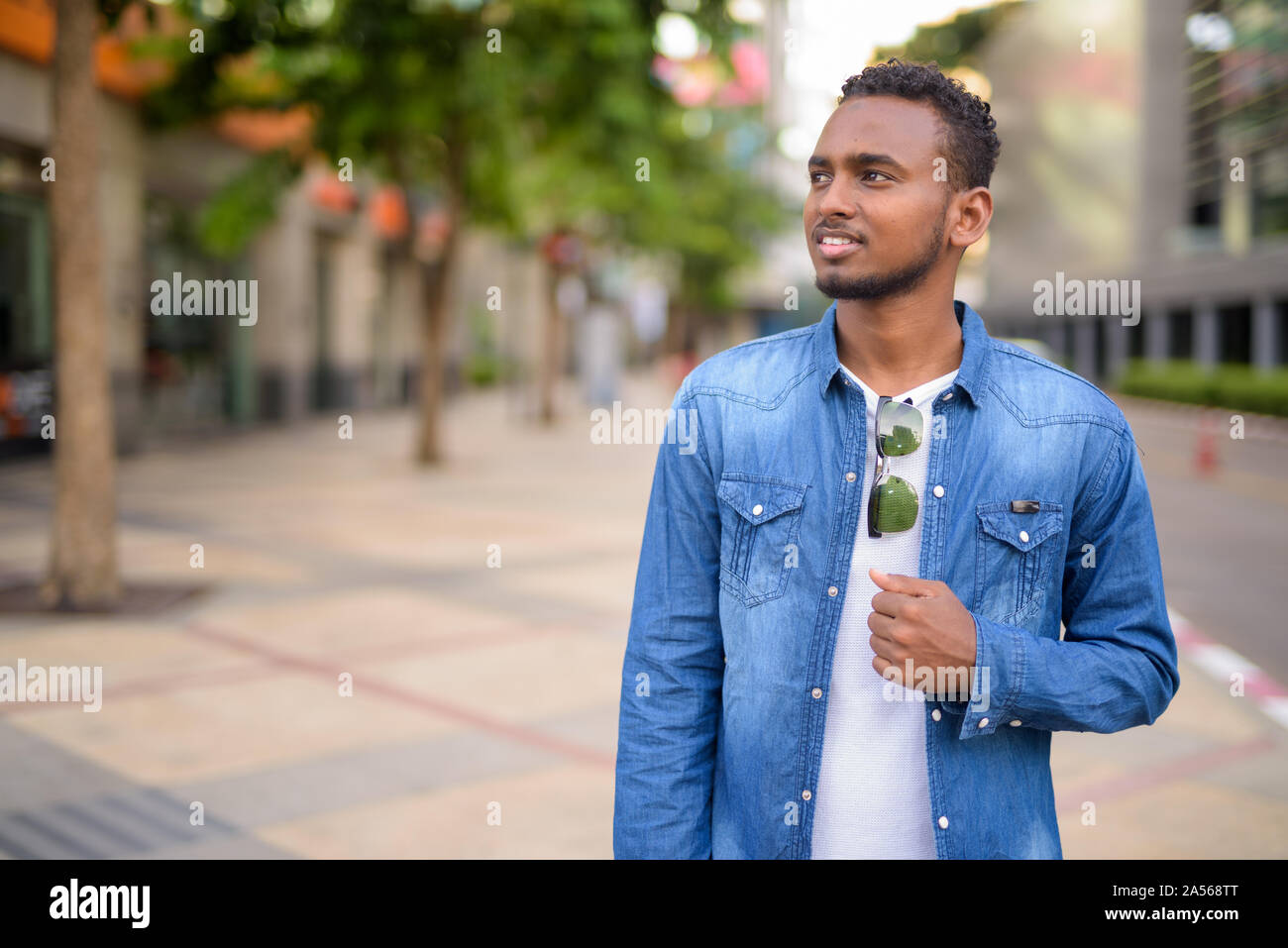 Happy young African bearded man with Afro hair thinking in the city ...
