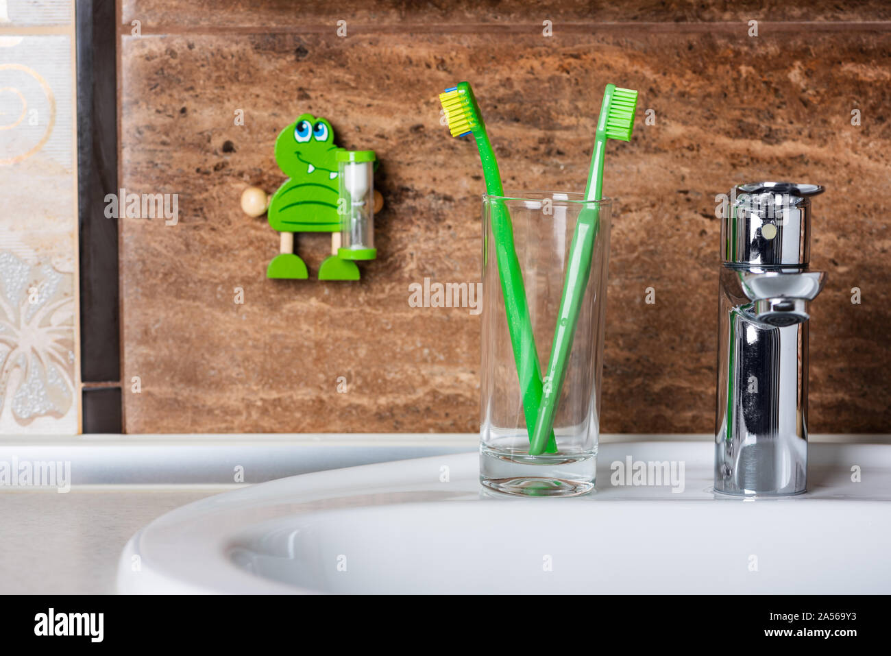 Original and orthodontic toothbrushes in glass and timer on wall ...