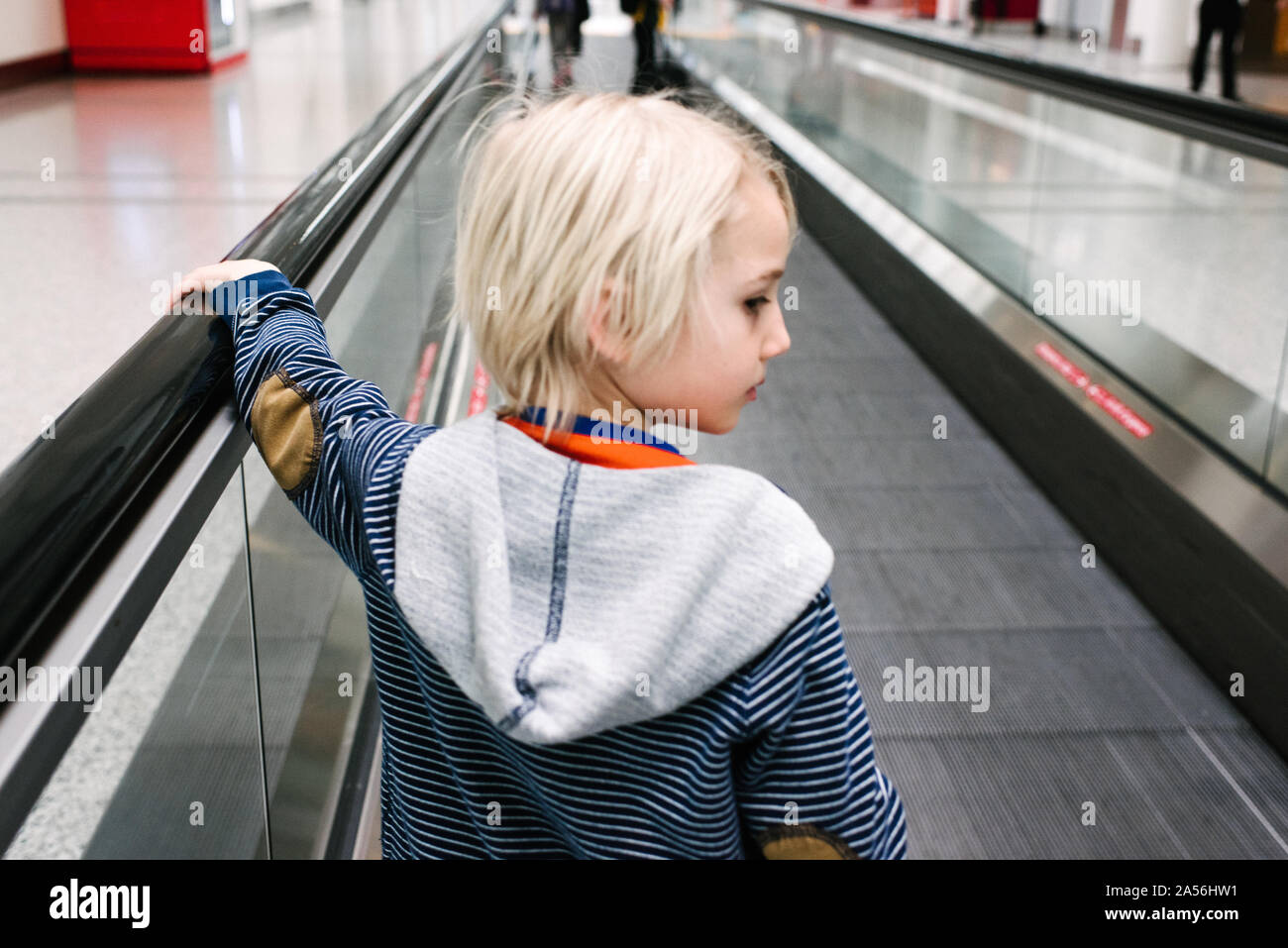 Blond haired boy on airport moving walkway looking over his shoulder ...