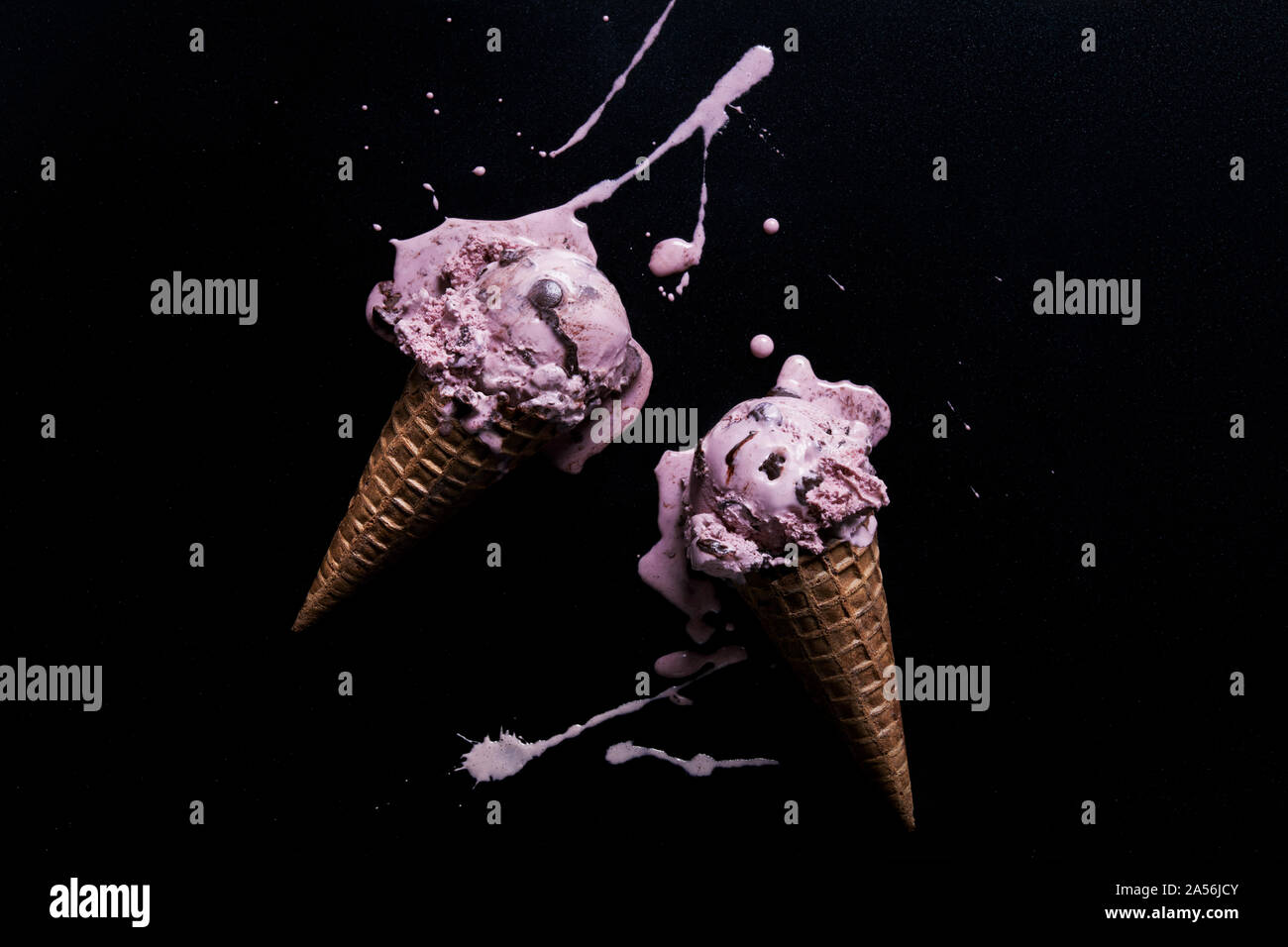 Two chocolate chip raspberry ice-cream cones with melted splash against ...