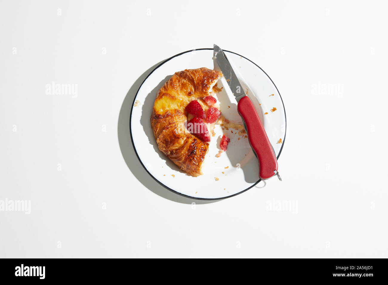 Strawberry danish pastry on plate with swiss army knife, overhead view ...