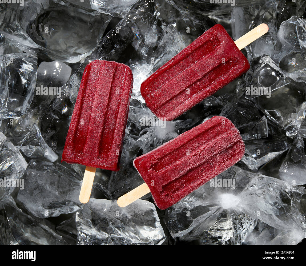 Three homemade raspberry iced lollies melting on chunks of ice ...