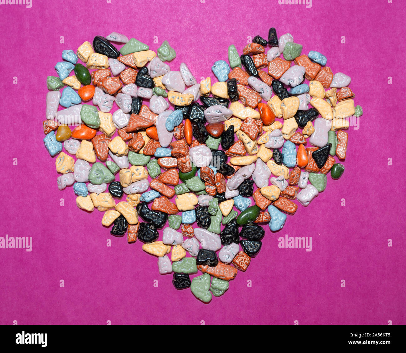 Love concept.Heart-shaped decoration from colorful pebbles on a pink ...