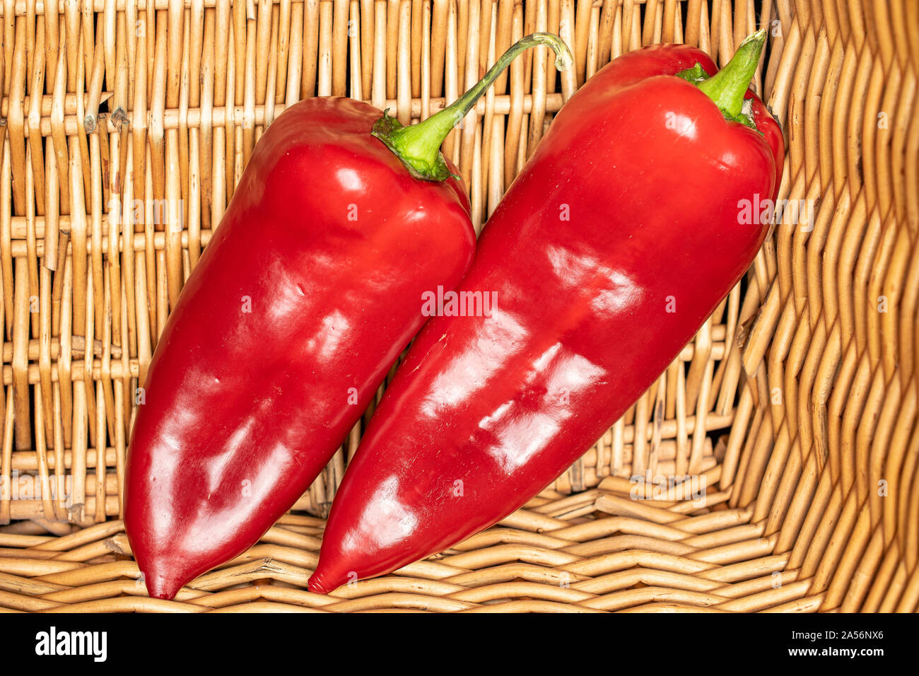 Group of two whole sweet red bell pepper with braided rattan behind ...