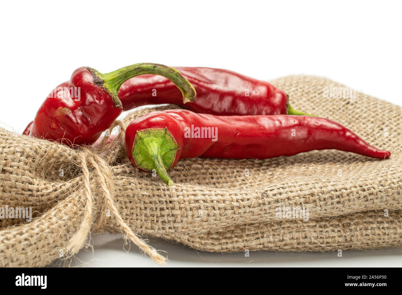 Group of three whole dark red fresh hot pepper with jute bag isolated ...