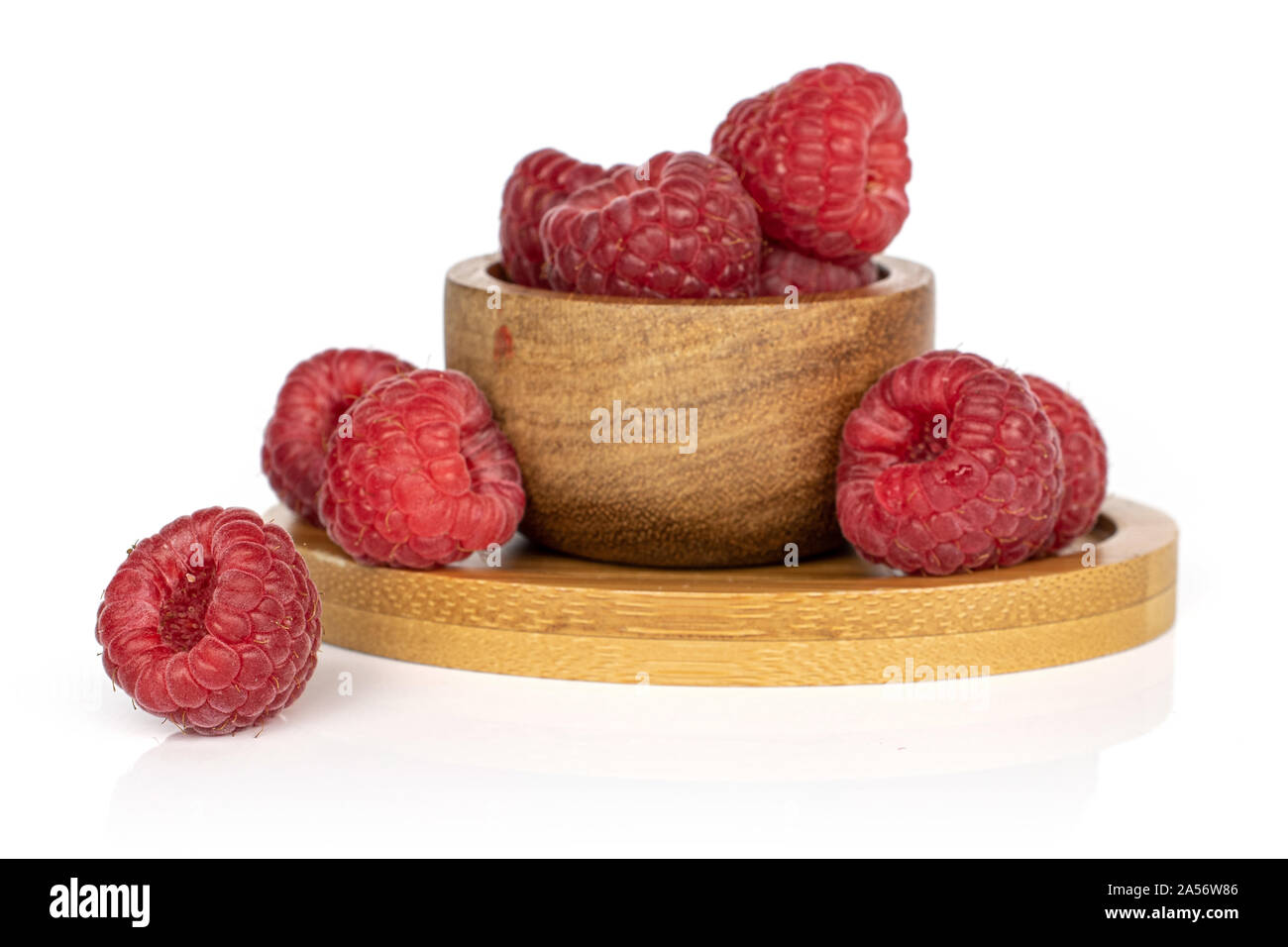 Lot of whole fresh red raspberry on round bamboo coaster in bamboo bowl ...