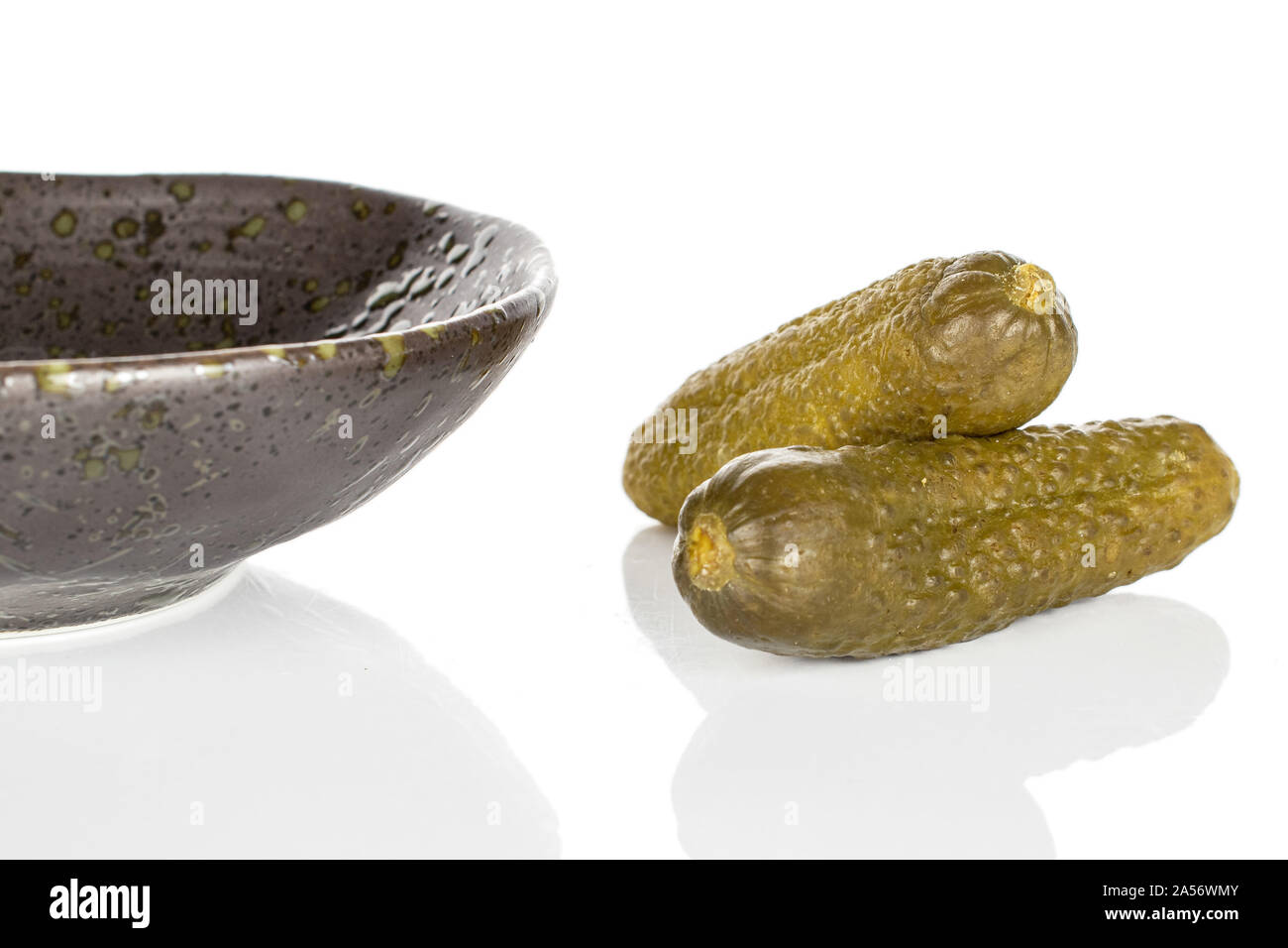 Group of two whole sour green pickle crossed on glazed bowl isolated on ...