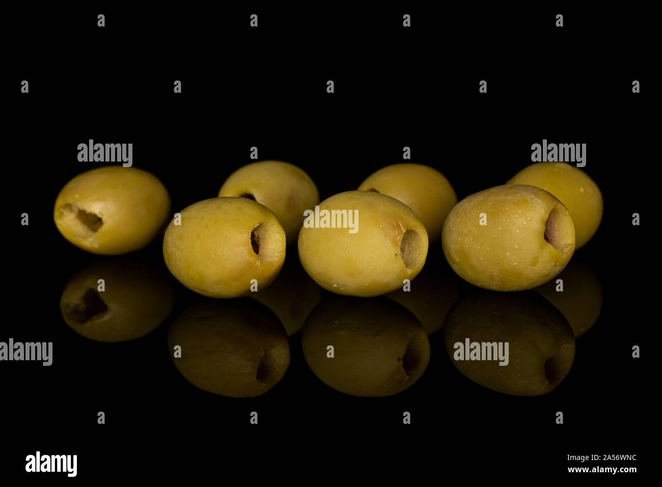 Group of seven whole marinated green olive isolated on black glass ...