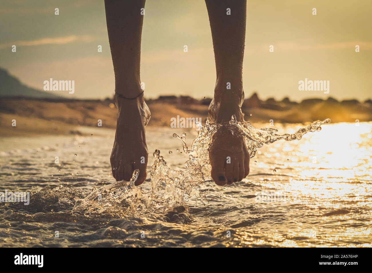 Girl's feet jumping on sea water. With some drops splashing, at dawn ...
