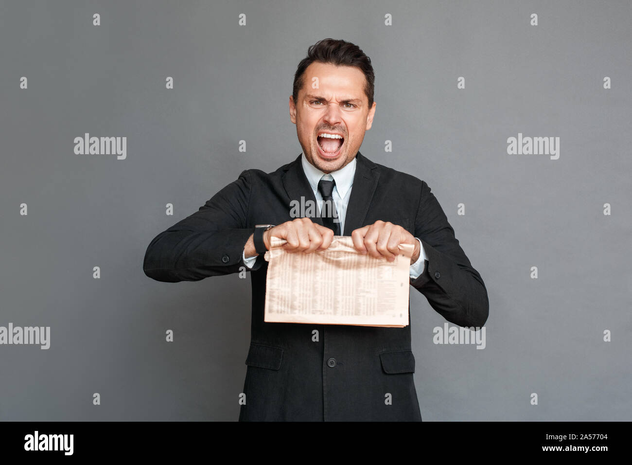 Businessman studio standing isolated on grey tearing newspaper into ...