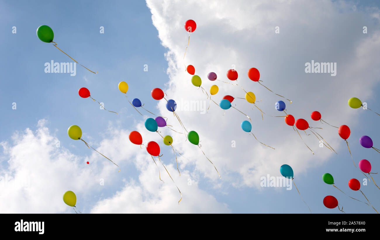 dozen of colored balloons in the sky with many white clouds symbol of ...