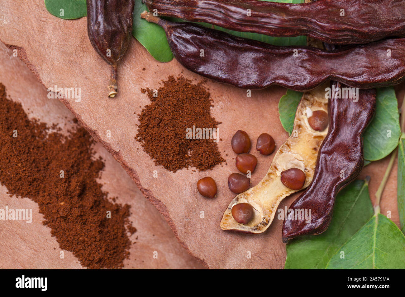 Carob. Organic carob pods with seeds and leaves on tree bark table ...