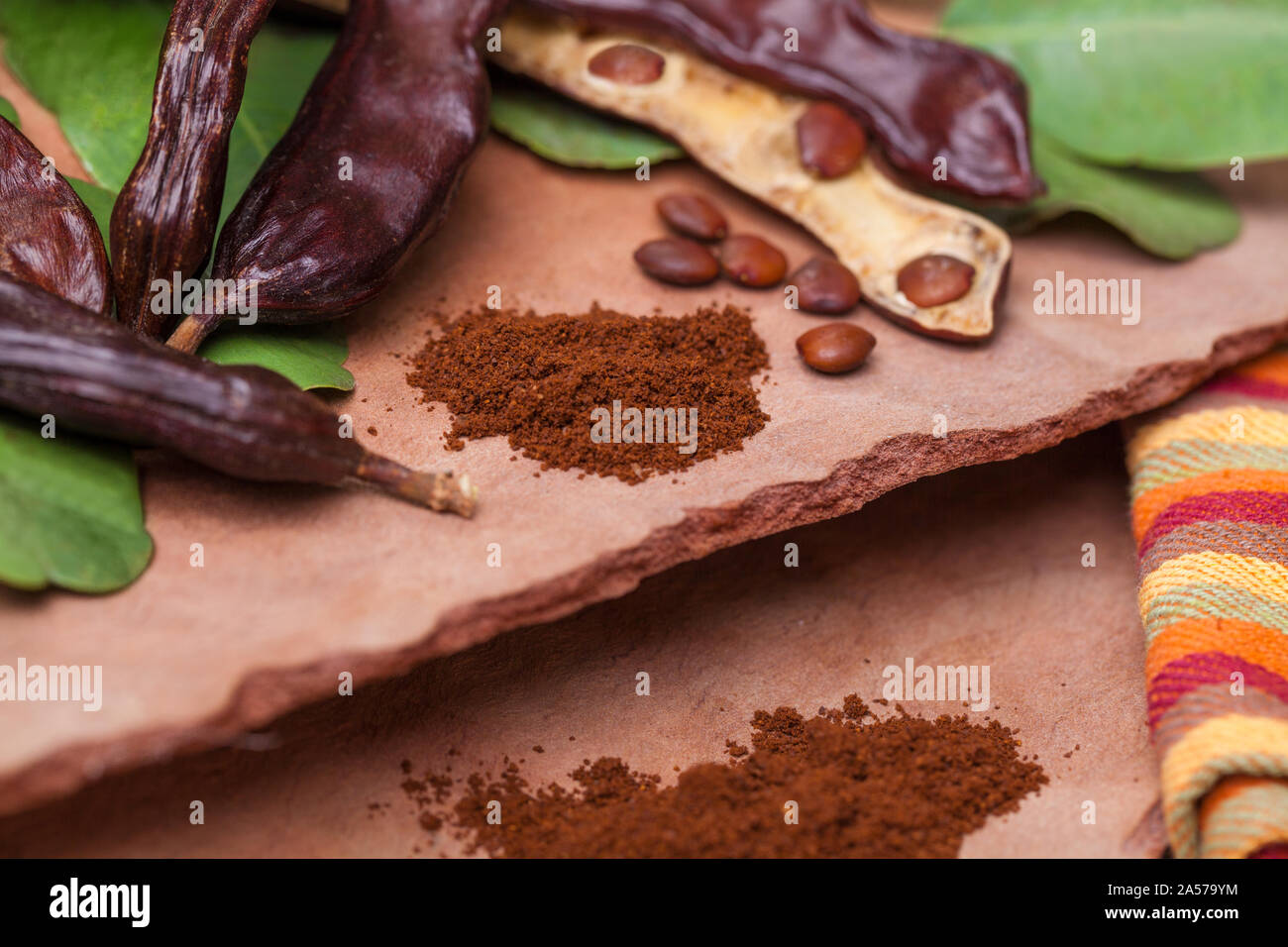 Carob. Organic carob pods with seeds and leaves on tree bark table ...