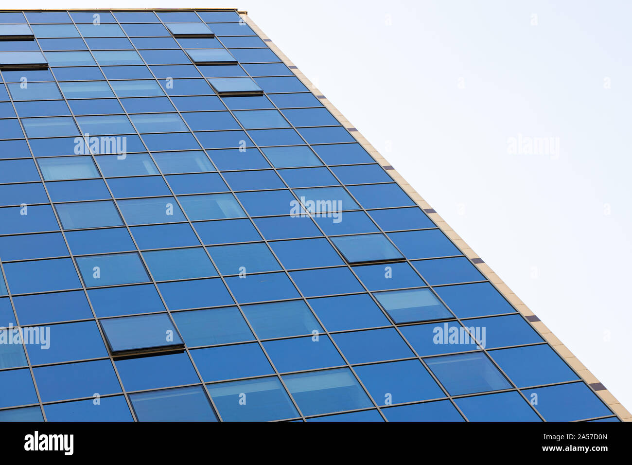 Ground view of blue glass surface of building wall reflecting blue sky ...