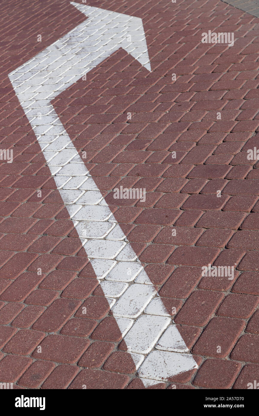 Close-up of white road marking arrow pointing to right on maroon paving ...