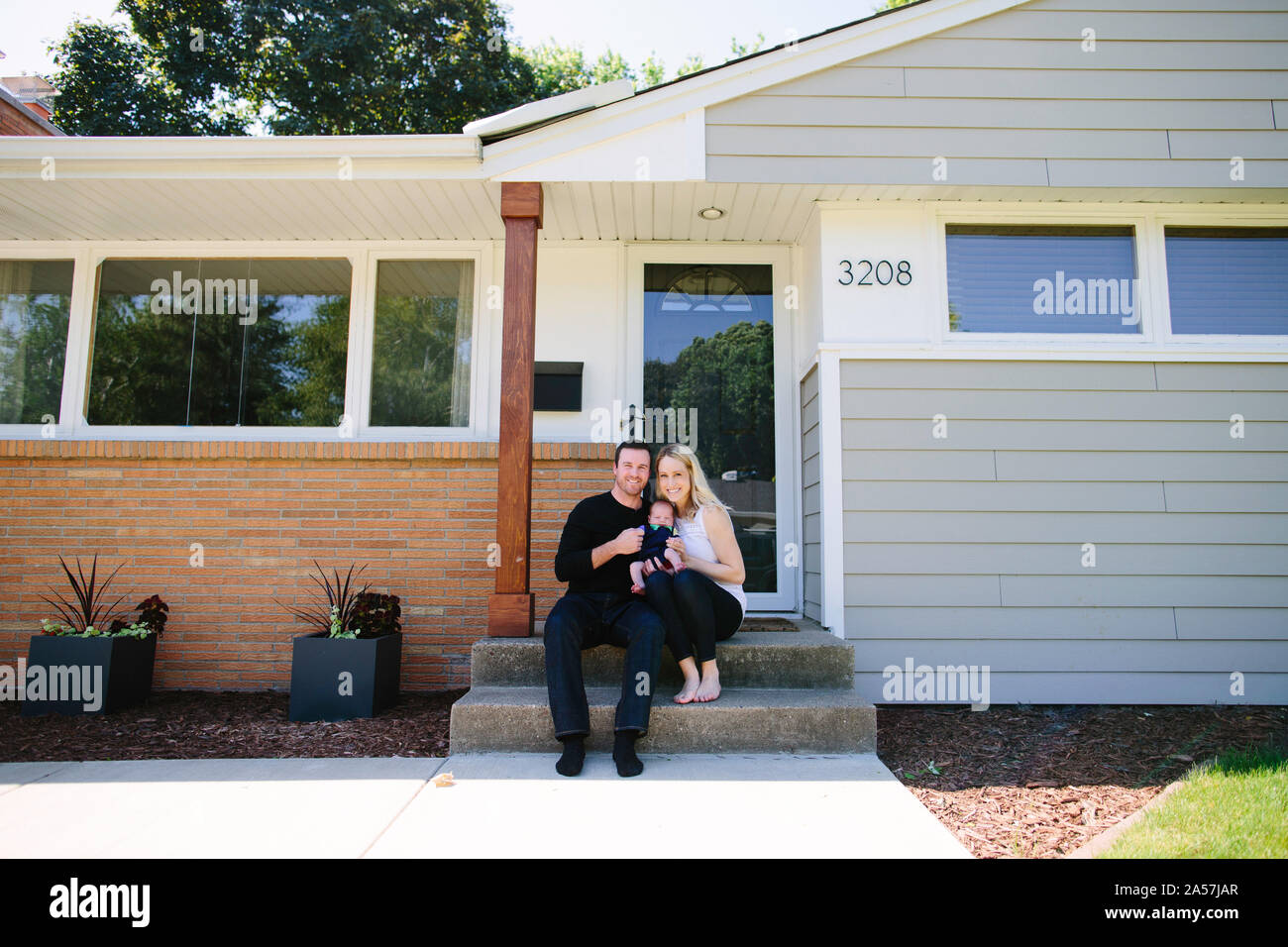 New parents sit on the front stoop of their home with their newborn ...
