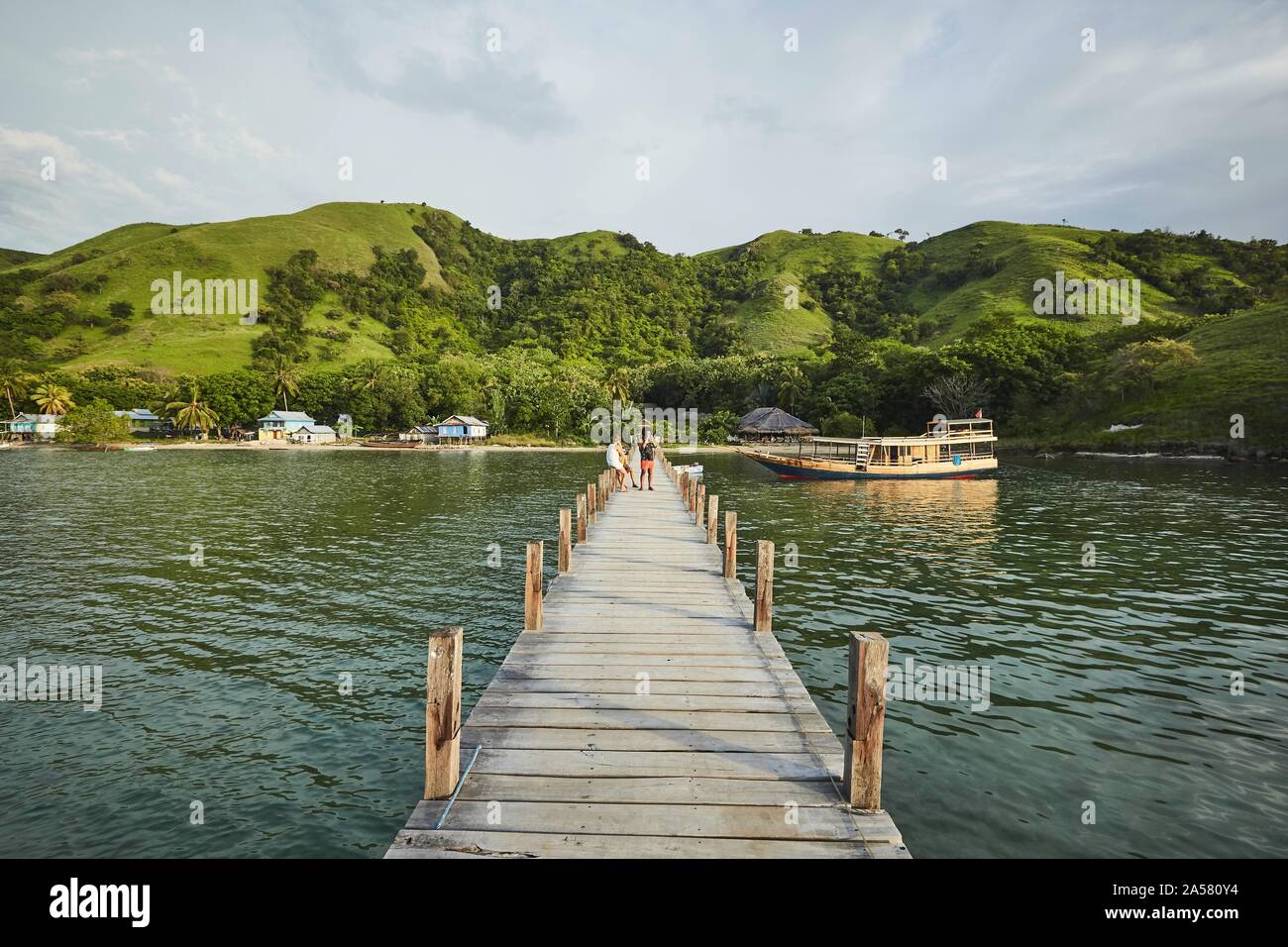 Wooden jetty in front of green hilly landscape with huts on the beach ...