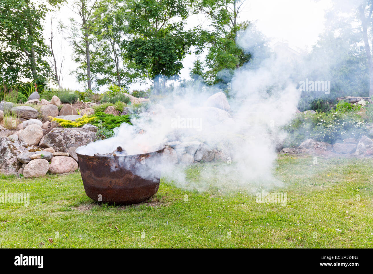 Smoking iron cauldron in a garden in summer Stock Photo - Alamy