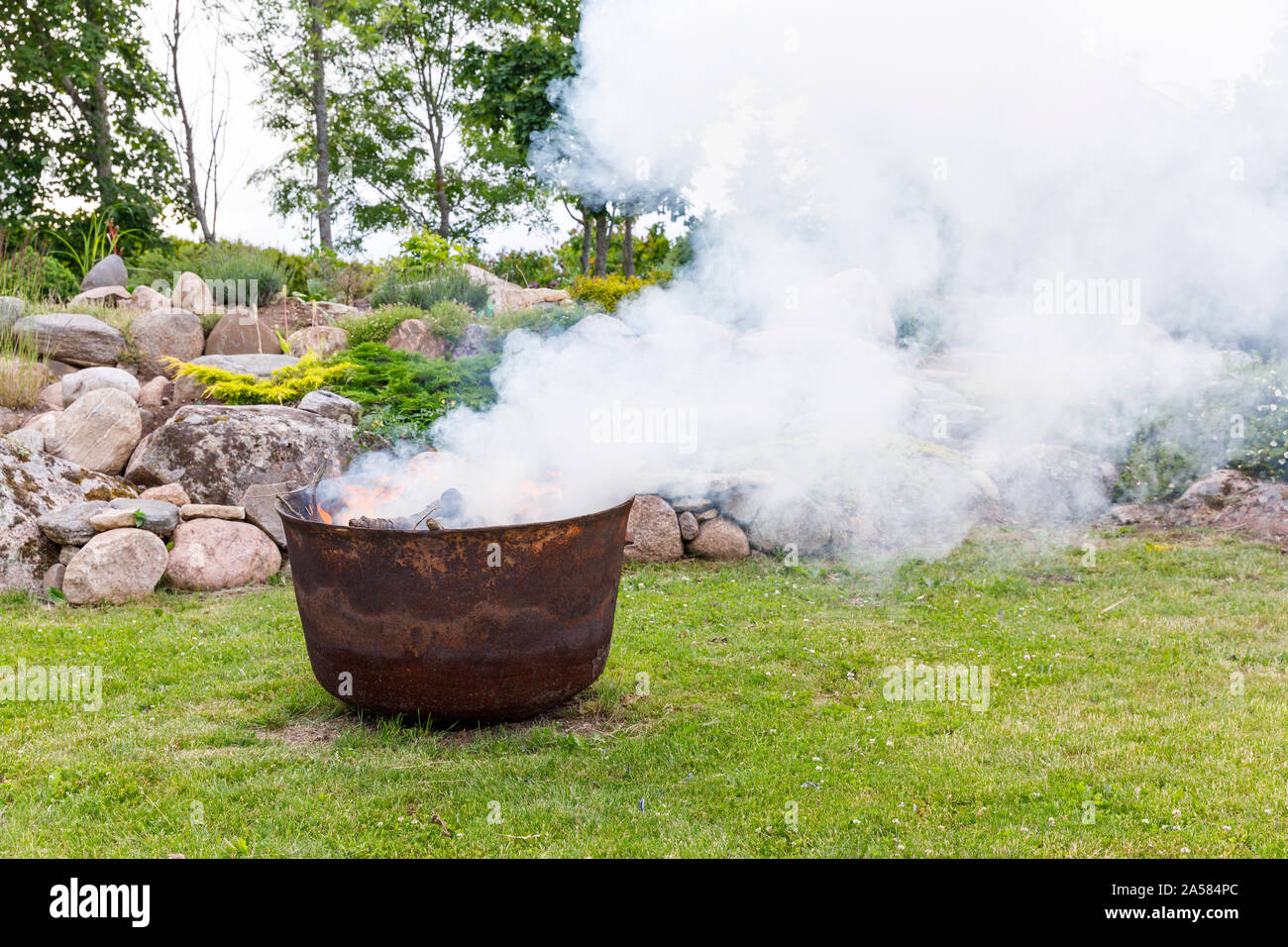 Smoking iron cauldron in a garden in summer Stock Photo - Alamy