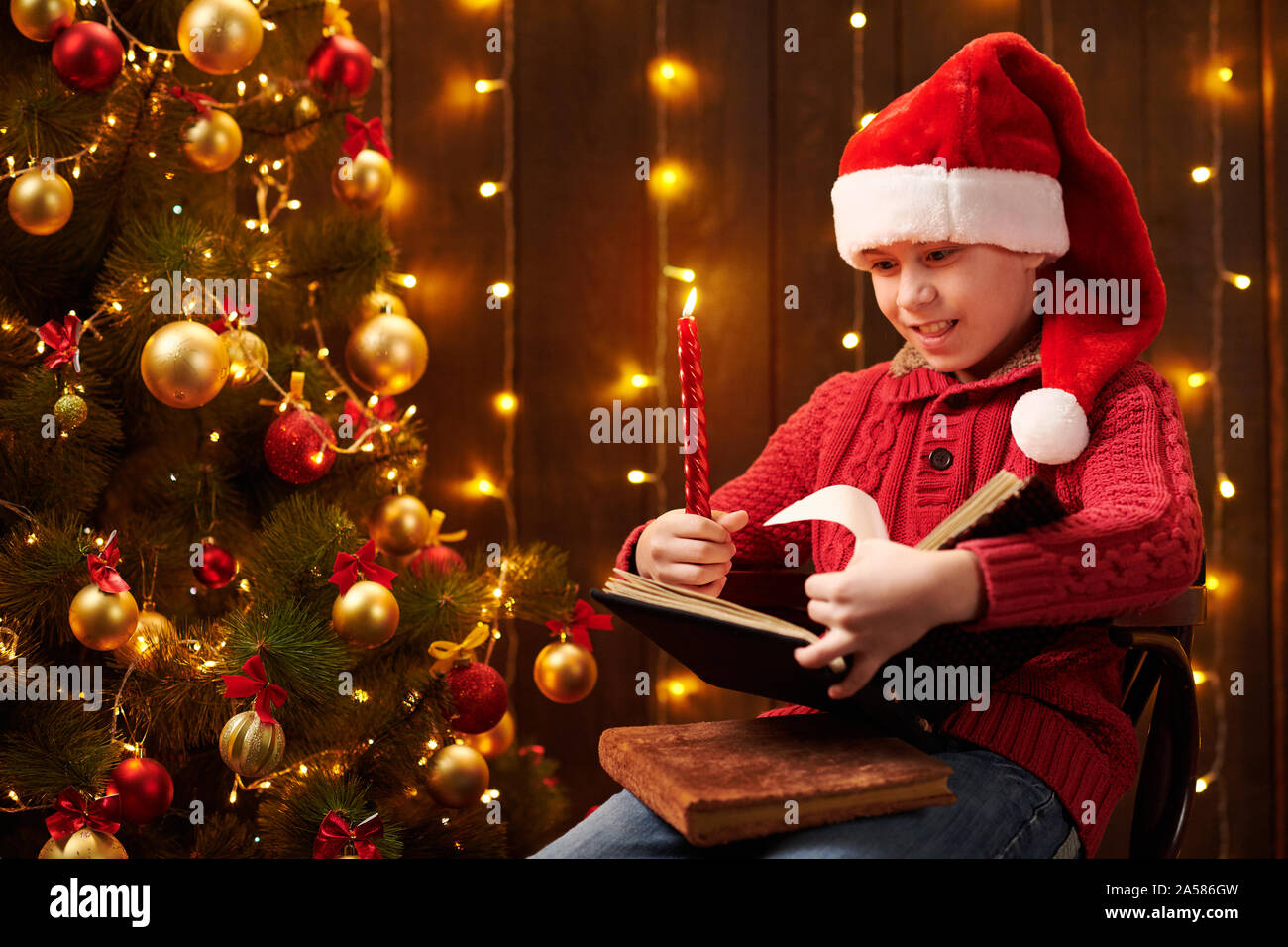 Teen boy reading book, sitting indoor near decorated xmas tree with ...