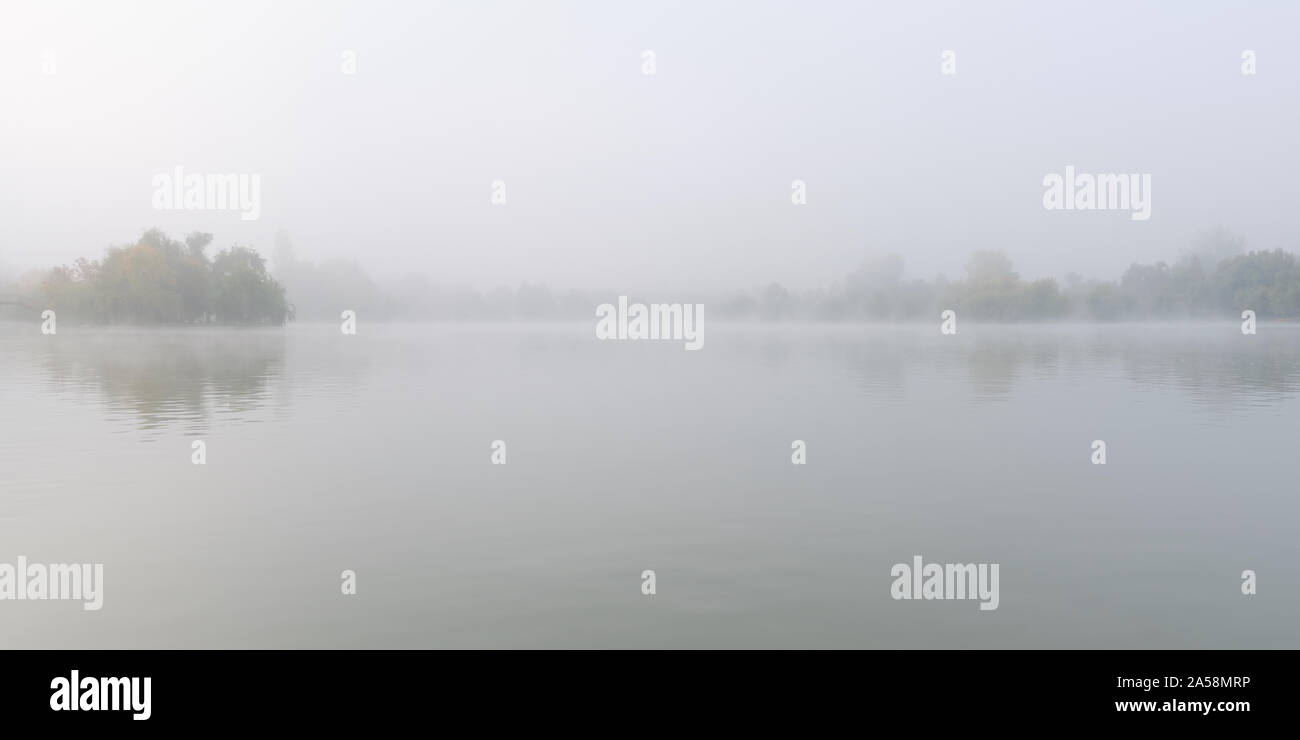 Panorama of lake with fog and faded tree silhouettes Stock Photo - Alamy