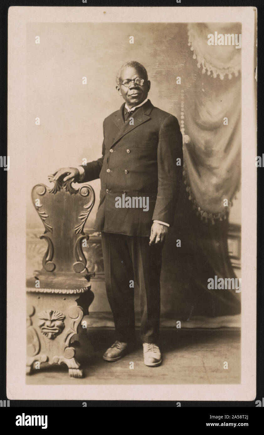 Unidentified man, facing front, standing next to chair, posing for full ...