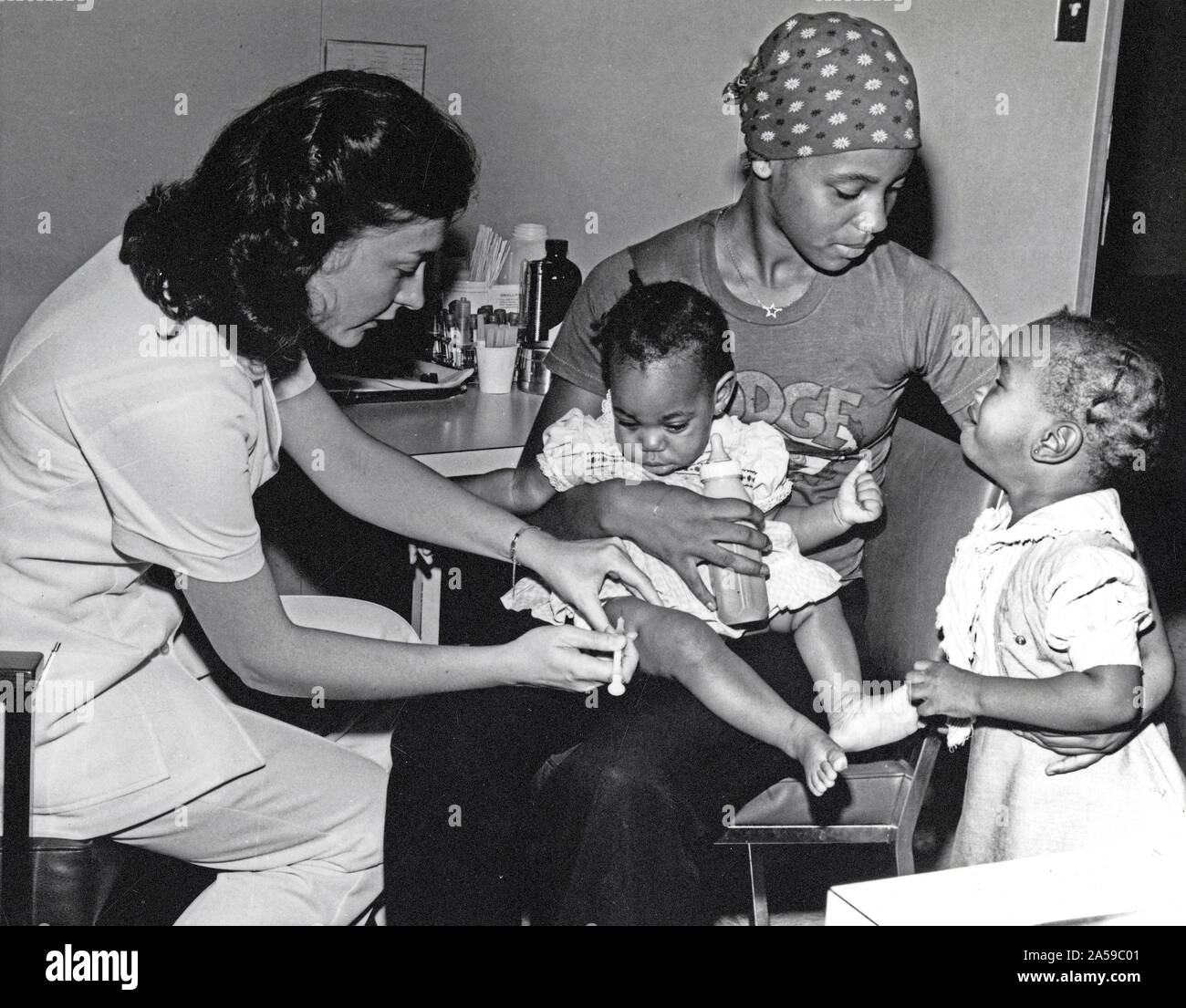 an African American child receives an injection in her leg just above ...