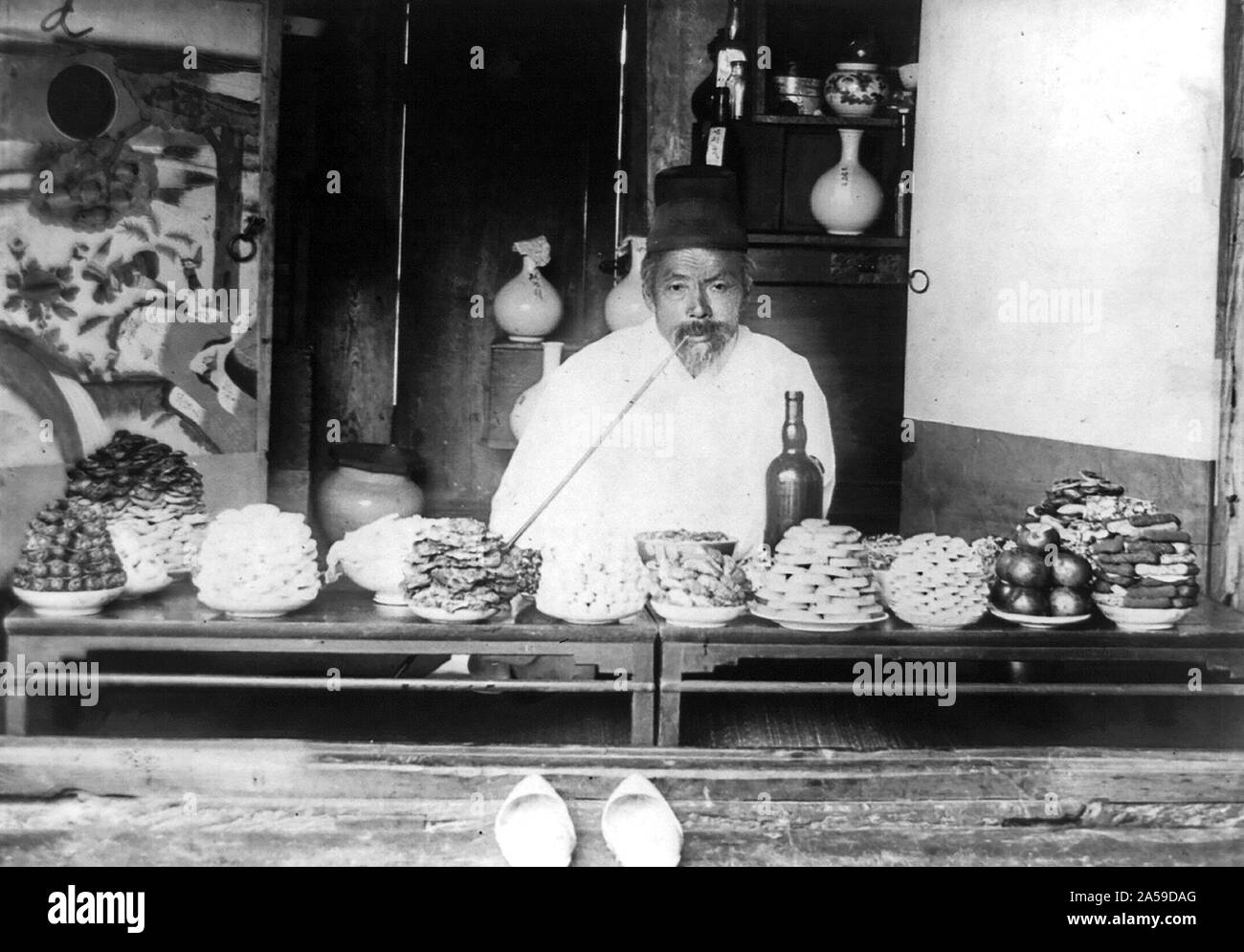Korean man smoking long pipe behind food on counter. 1890-1923 Stock ...