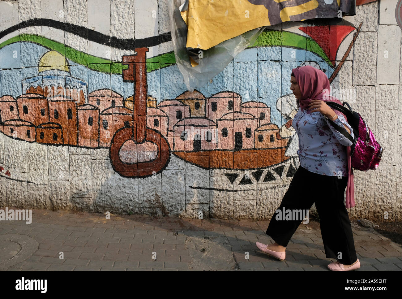 A Palestinian woman walks past a wall painting showing the "key of ...