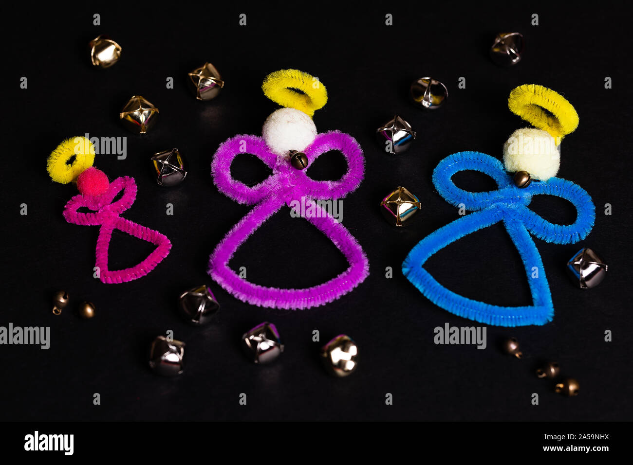 3 pipe-cleaner craft angels on a black background with several gold and ...