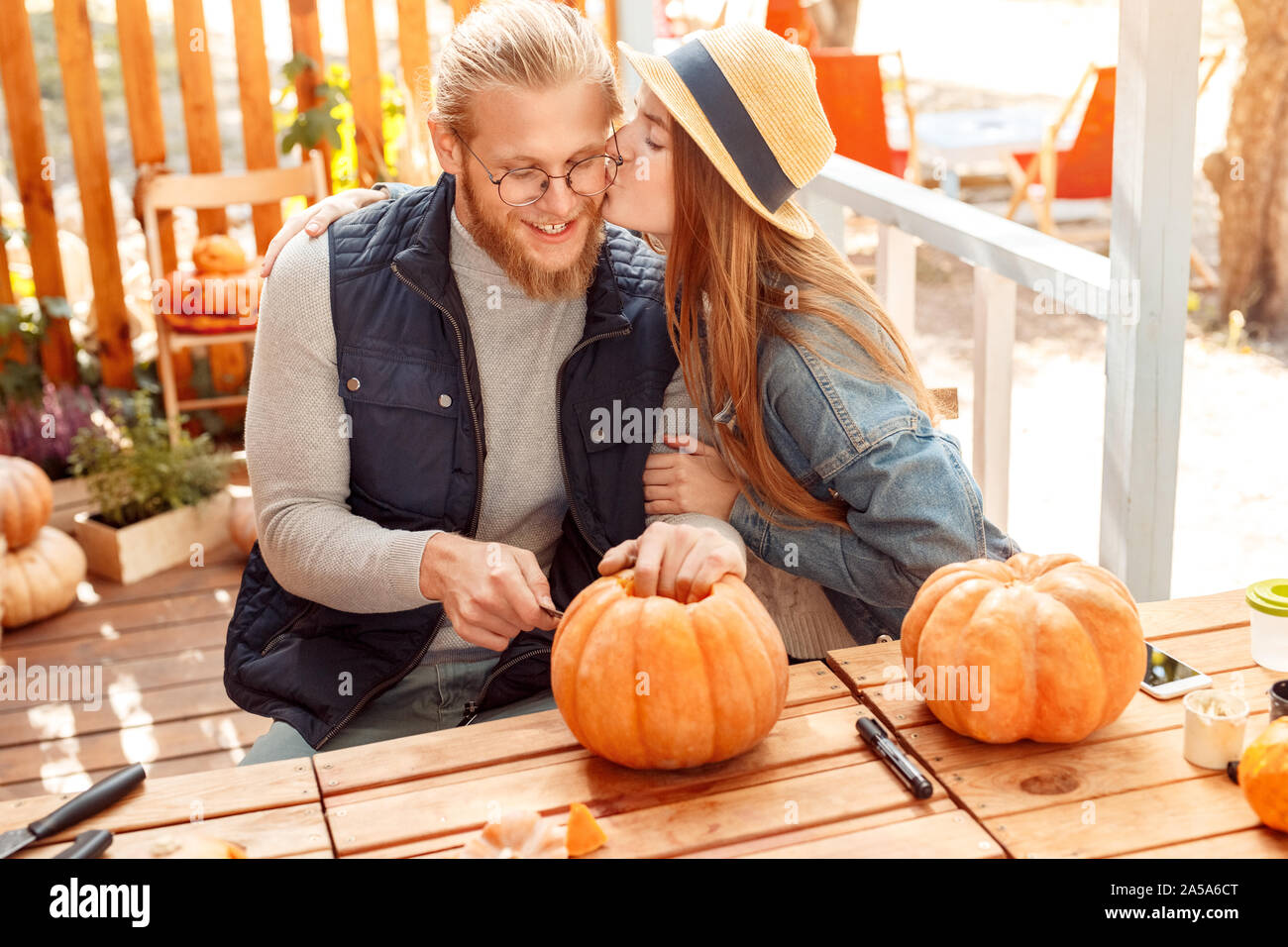Young adult woman kissing man while he carved pumpkin Stock Photo - Alamy