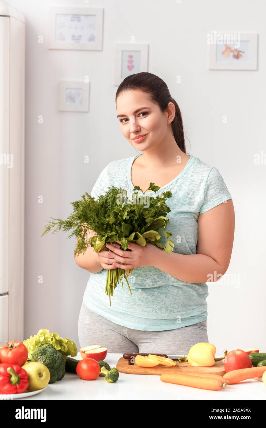 Cooking Meal. Chubby girl standing in kitchen with greenery looking ...