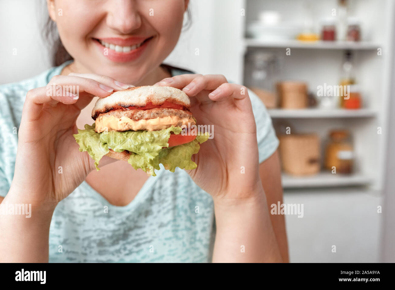Junk Food. Chubby girl sitting at kitchen eating hamburger smiling ...
