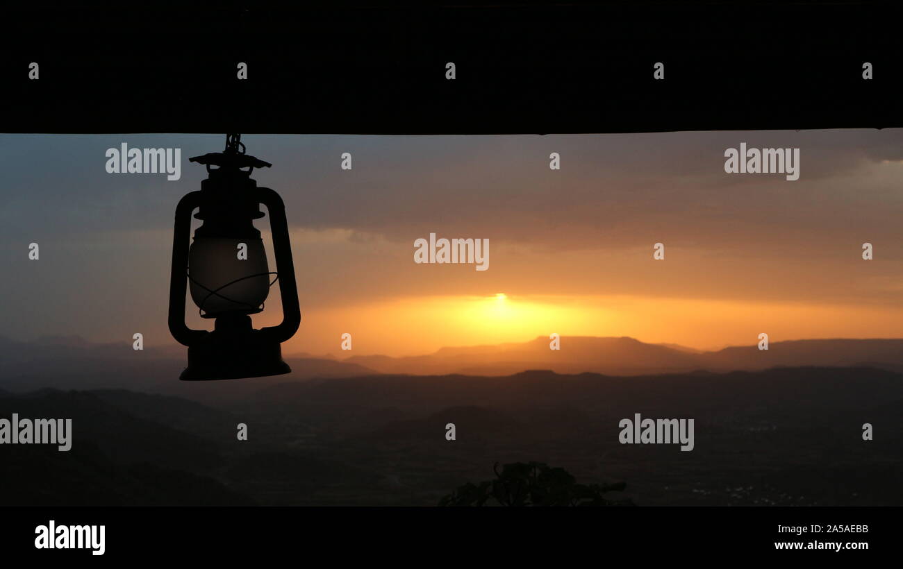 Paraffin oil lantern hanging from a beam silhouetted against a setting ...