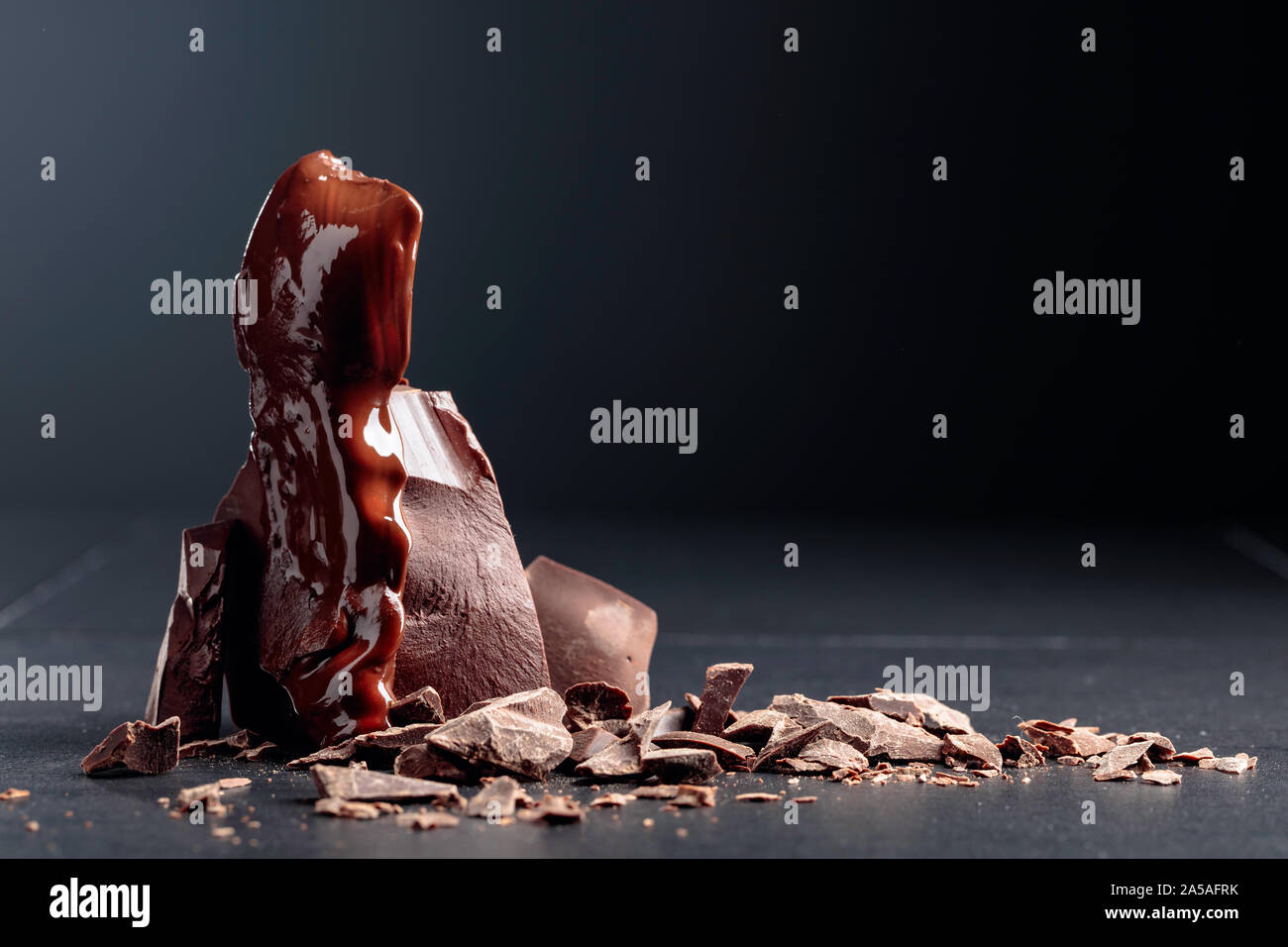 Broken large piece of dark chocolate with crumbs on a black table ...