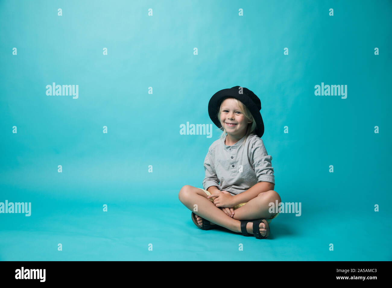 A boy on a blue background sits in a black hat and looks at the camera ...
