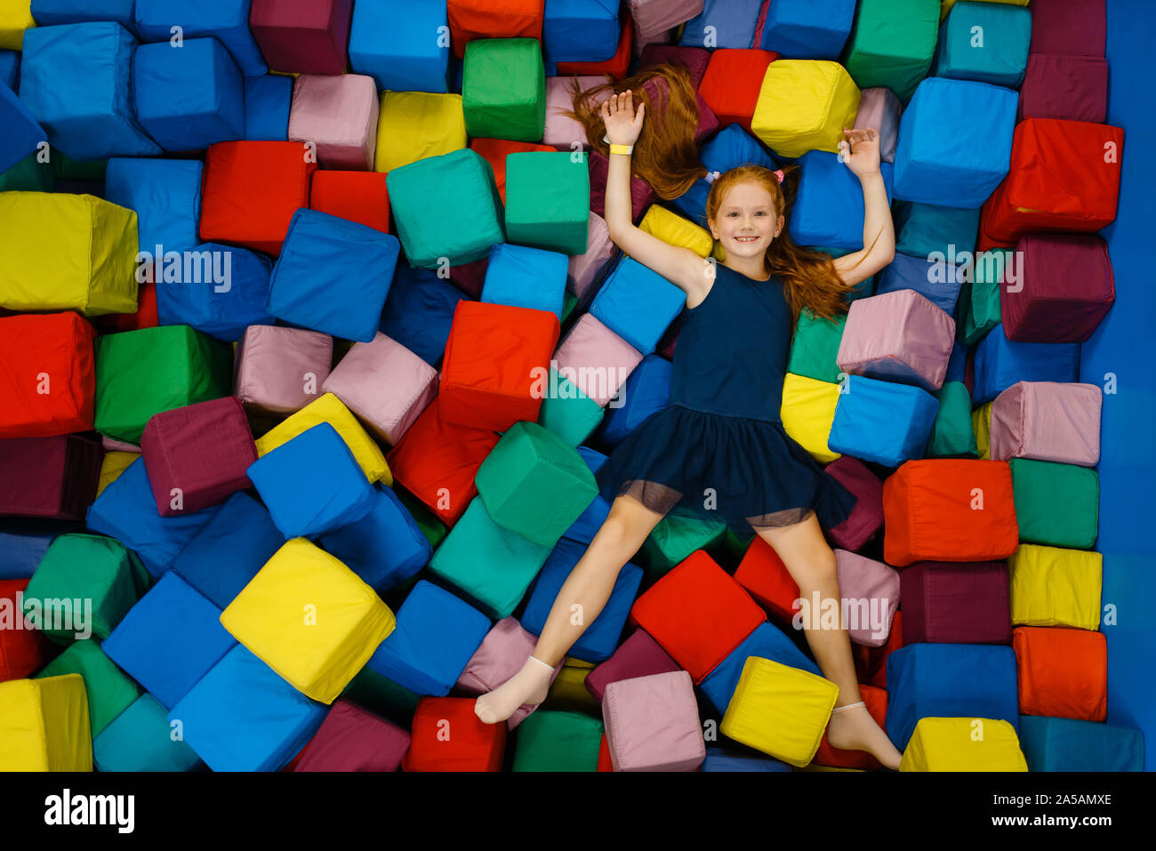 Cute little girl lying in soft cubes, playground Stock Photo - Alamy